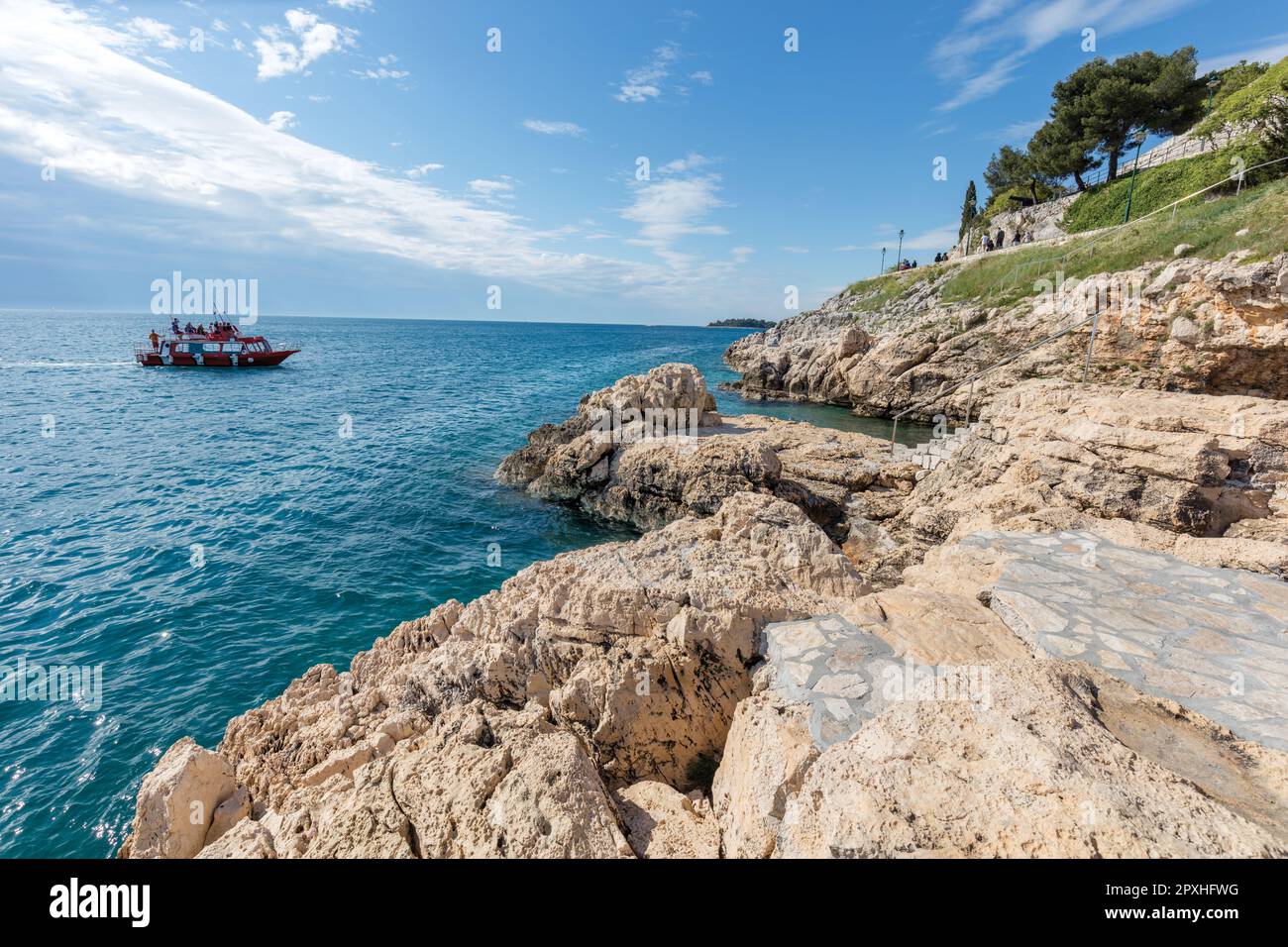 Tourist dive boats pass rocky coastline by promenade and beach at Plaza ...