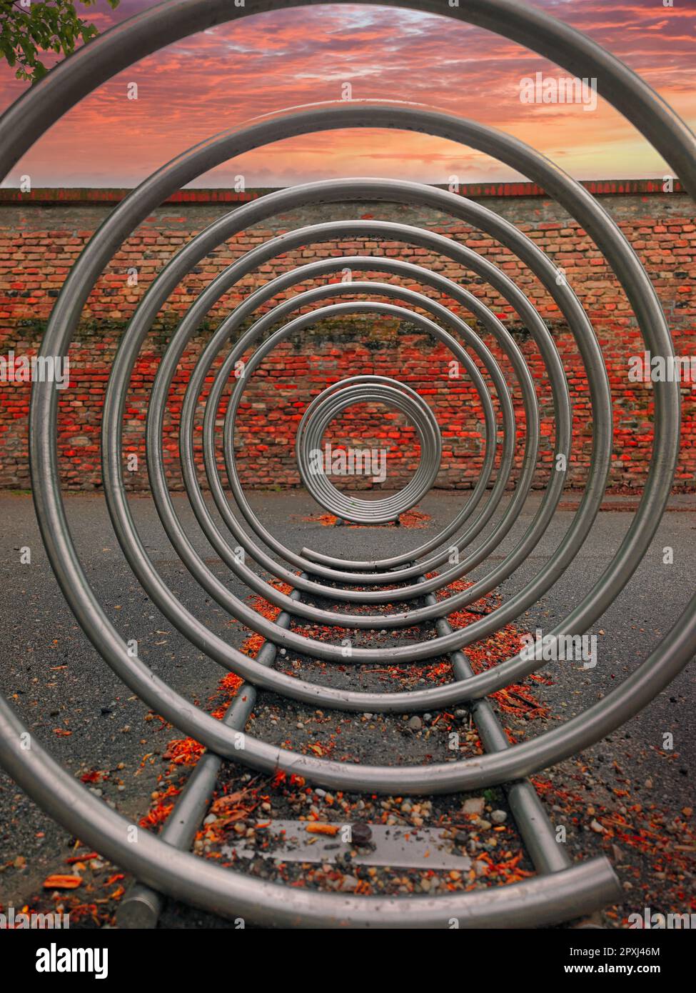 A vertical closeup of a metallic spiral object on a pathway against a ...