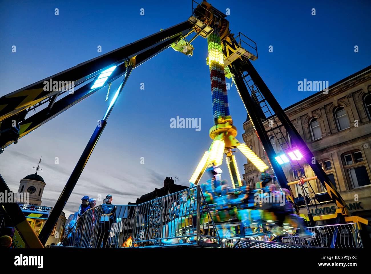 Fairground thrill ride, with people hoisted high on a crane arm and ...