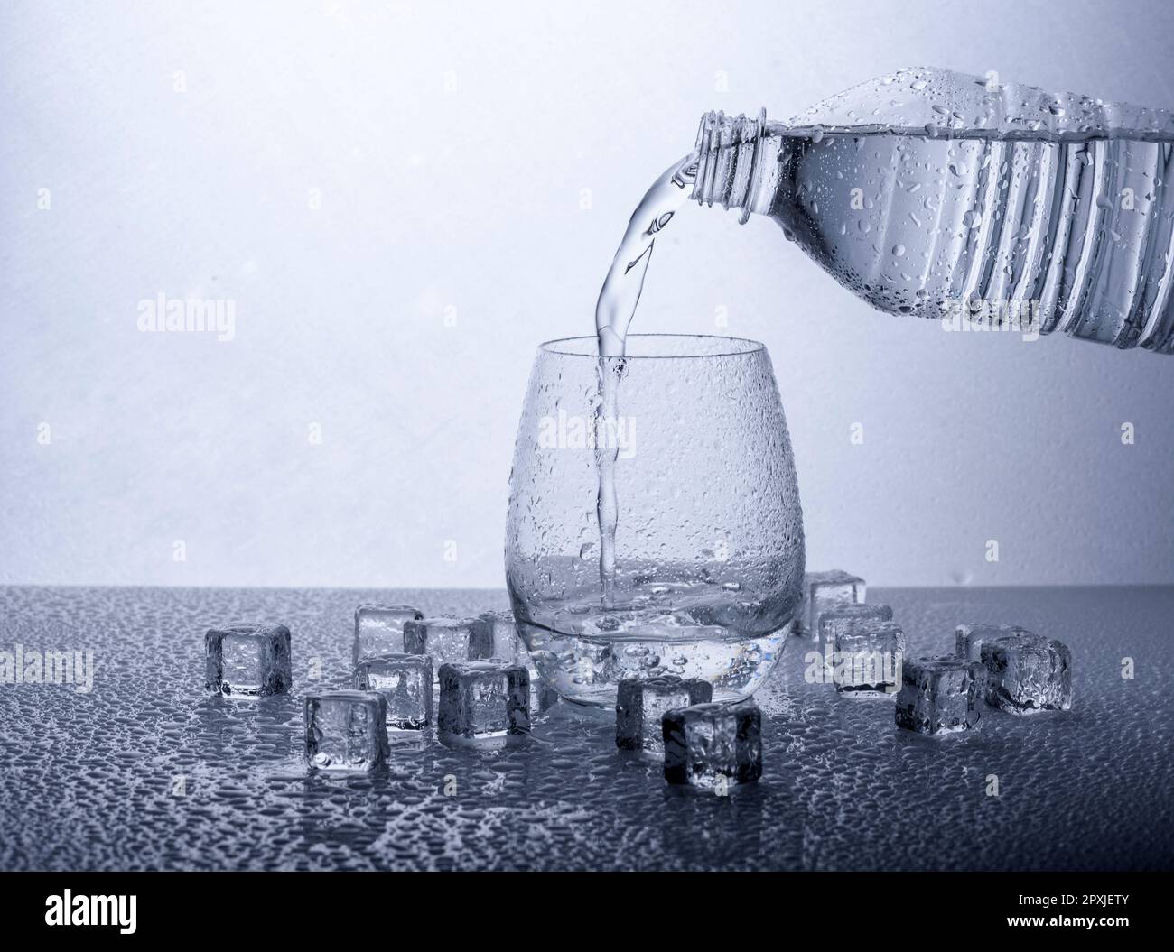 Pouring fresh drinking mineral water from plastic bottle. Glass filled with water over white ...