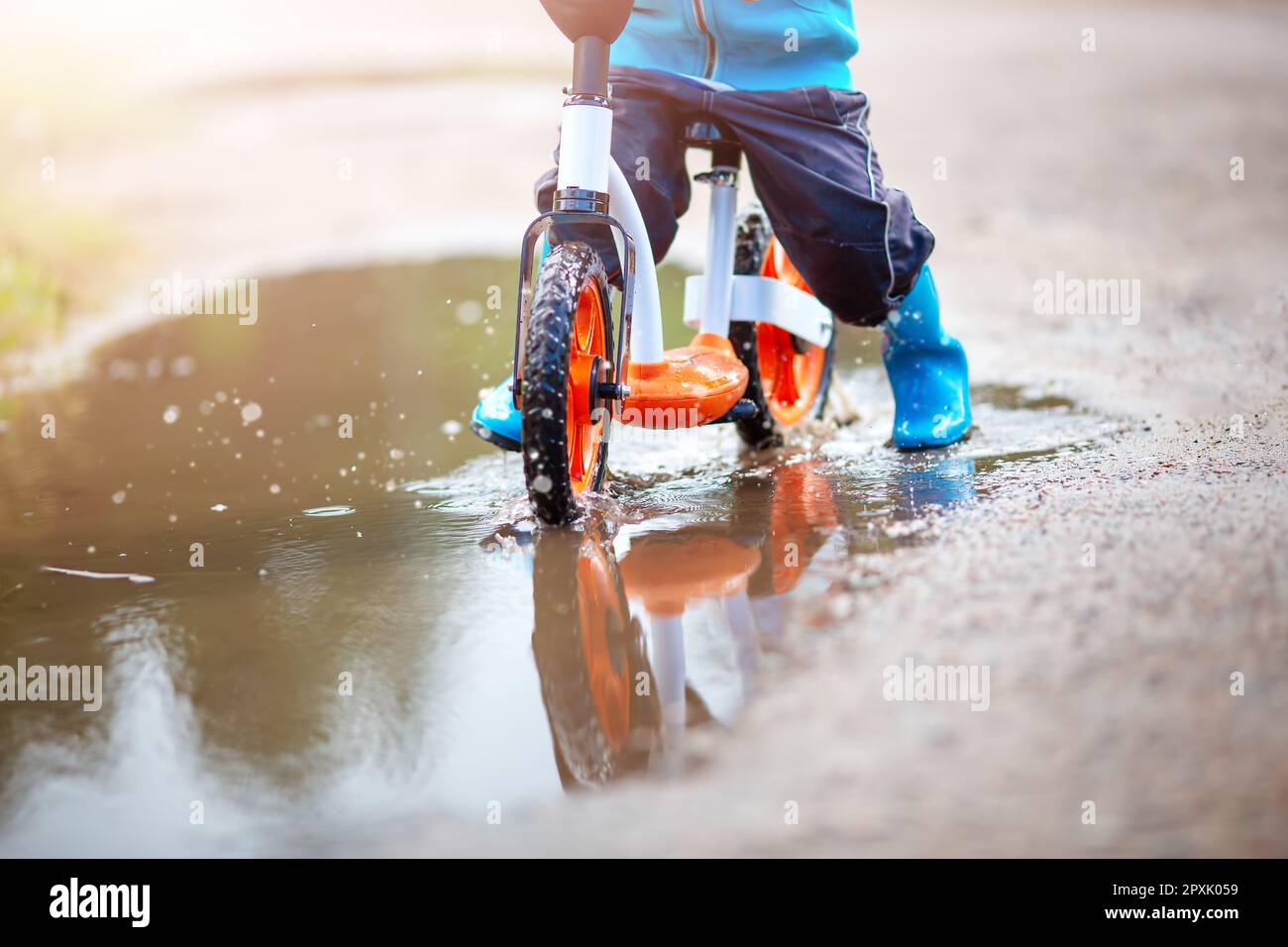 Child on the balance bike riding through the puddle. Concept of the ...