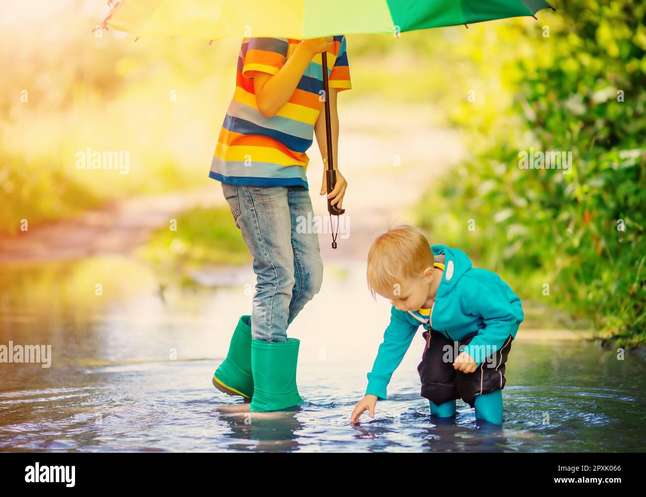 Two brothers standing with rainbow umbrella in the puddle. Concept of ...