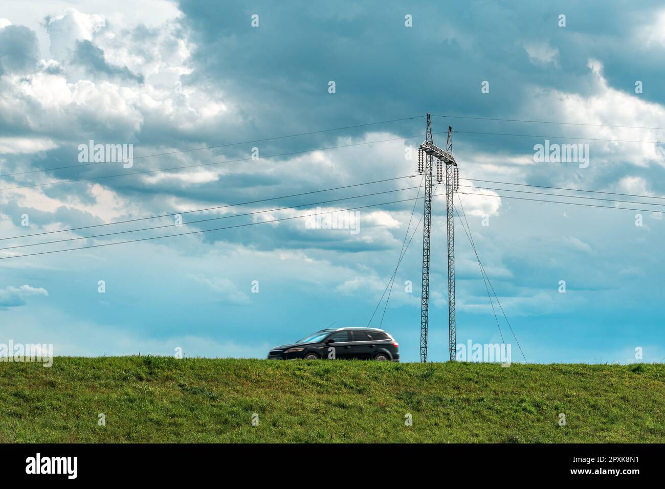 Speeding car on country road with electricity pylon in background ...