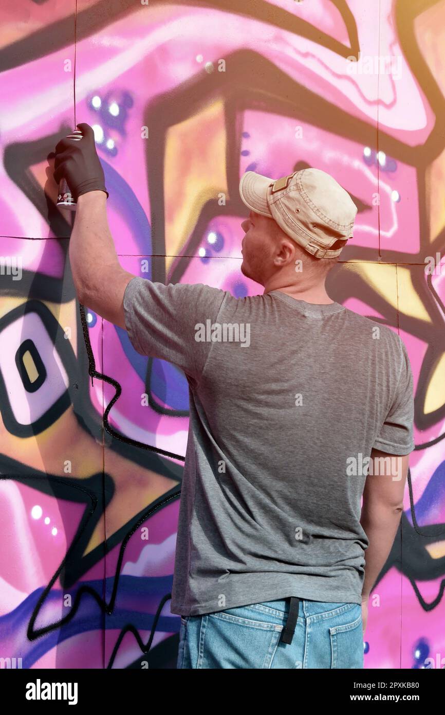 Young caucasian male graffiti artist drawing big street art painting in ...