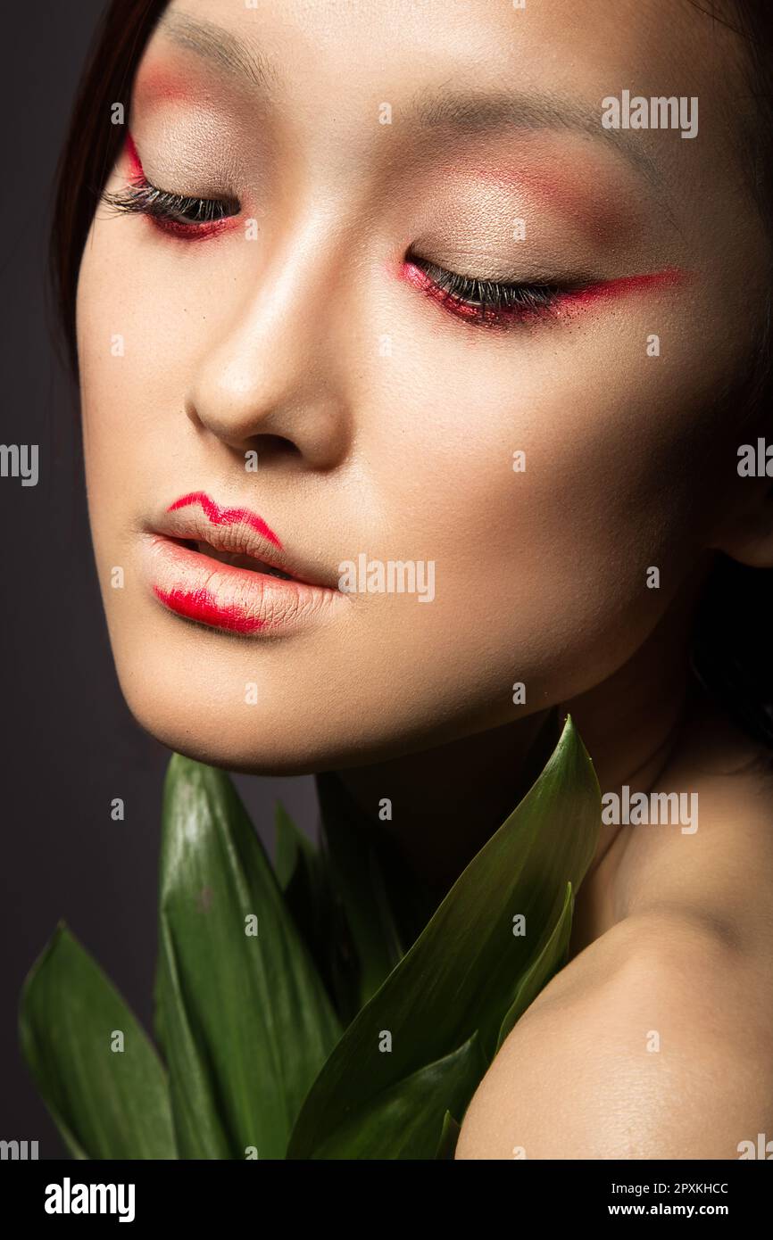 Beautiful Asian girl with a bright make-up art in green leaves. Beauty ...