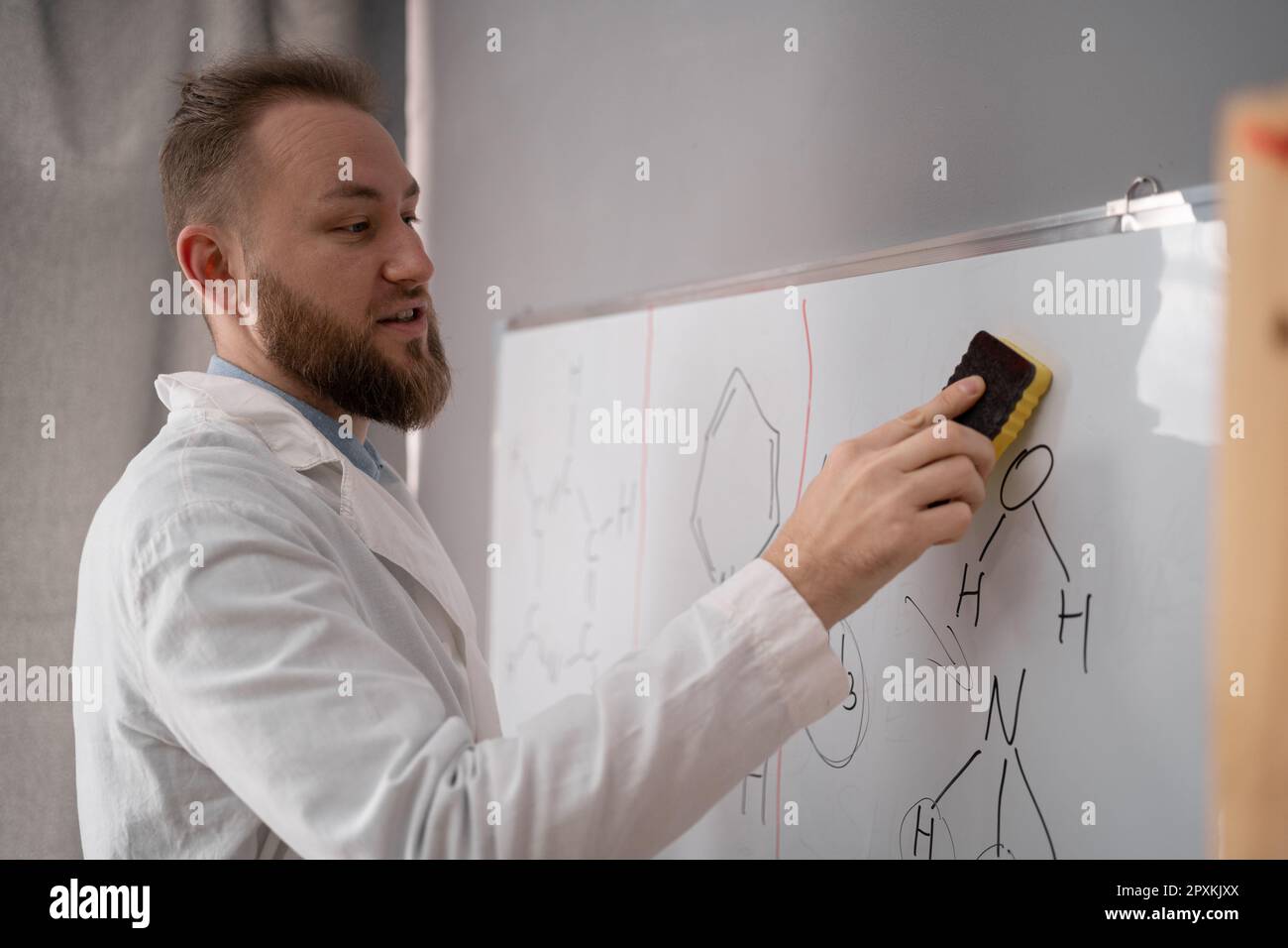 Teacher cleaning the whiteboard holding eraser erasing in classroom ...