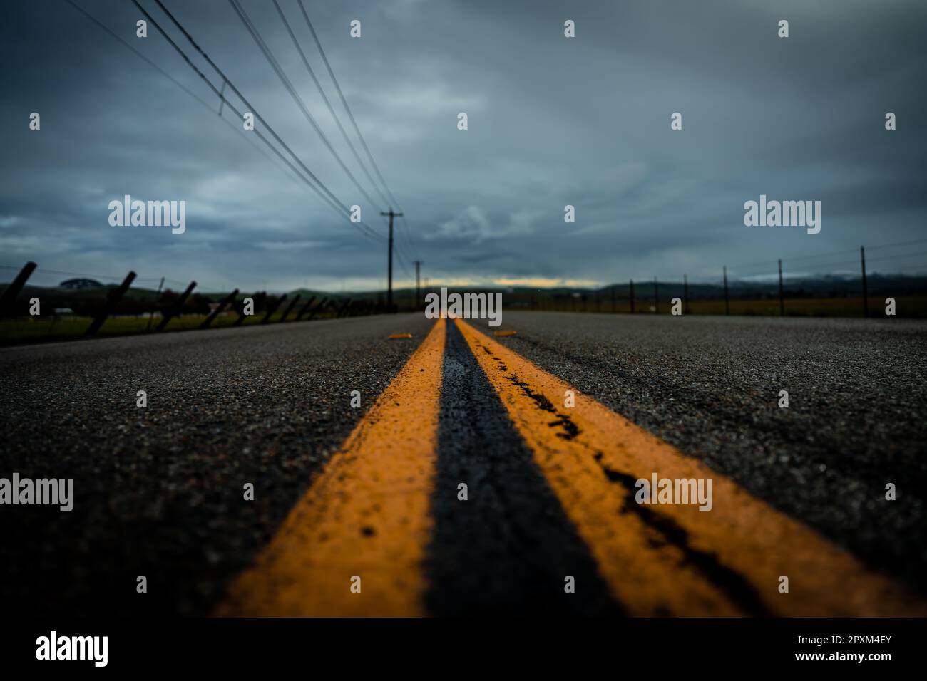 A winding two-lane road stretches out into the horizon on a stormy day ...