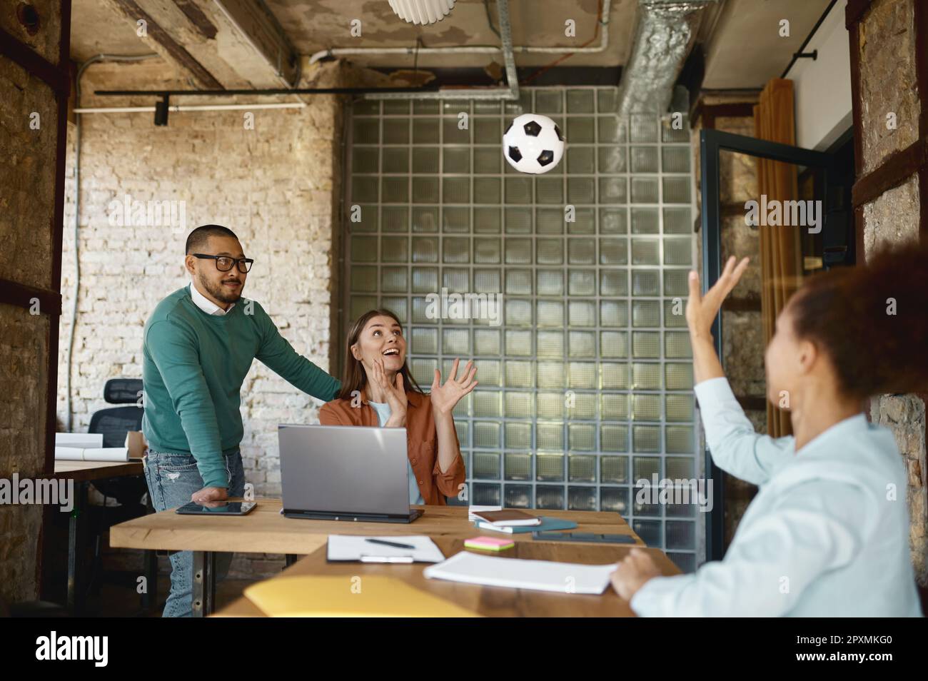 Young diverse multiethnic colleagues playing football in coworking ...
