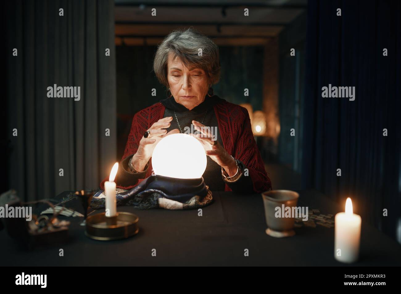 Portrait of old mature fortune teller looking into illuminated crystal ...