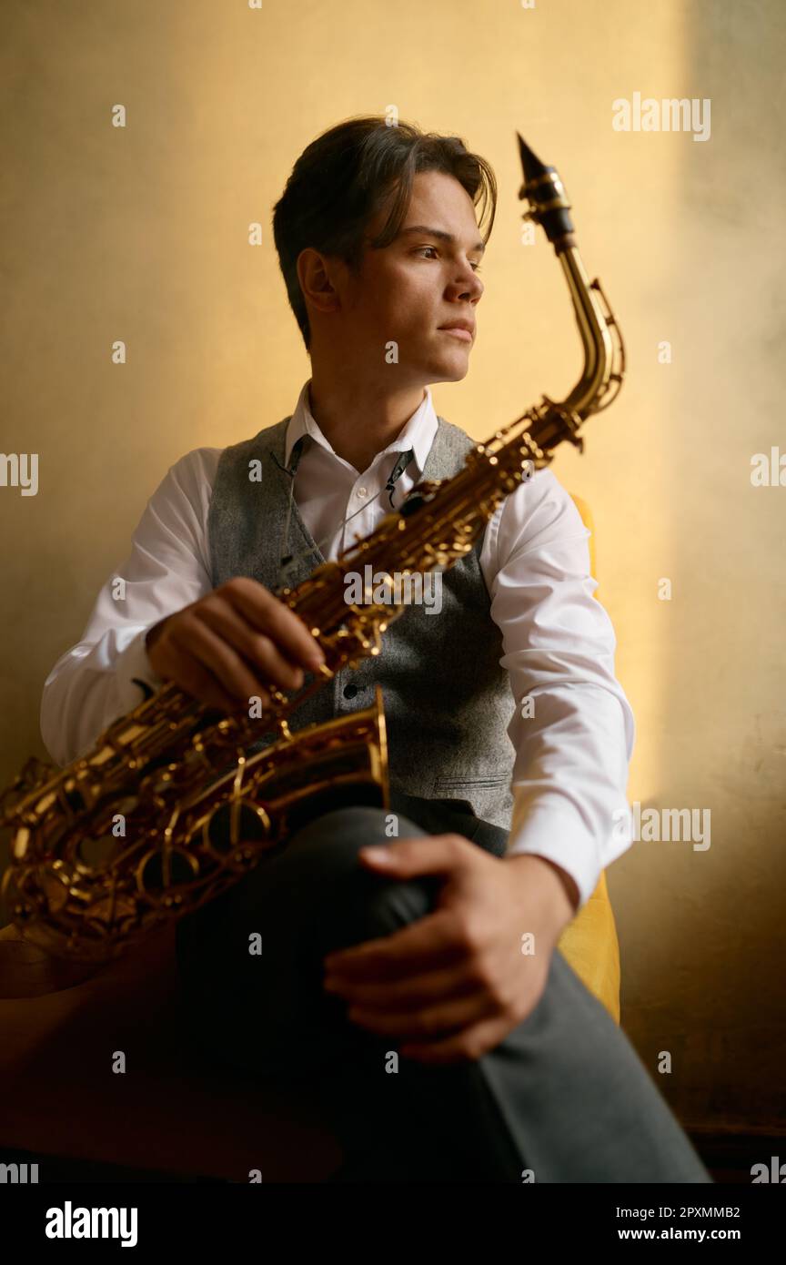 Young confident man rest in chair with saxophone under sunlight ...