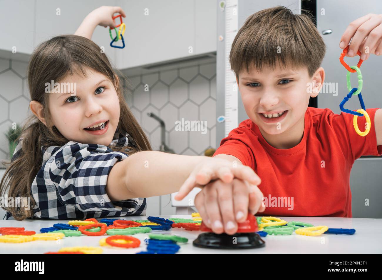 Portrait of two happy friends children sitting at table in kitchen at ...