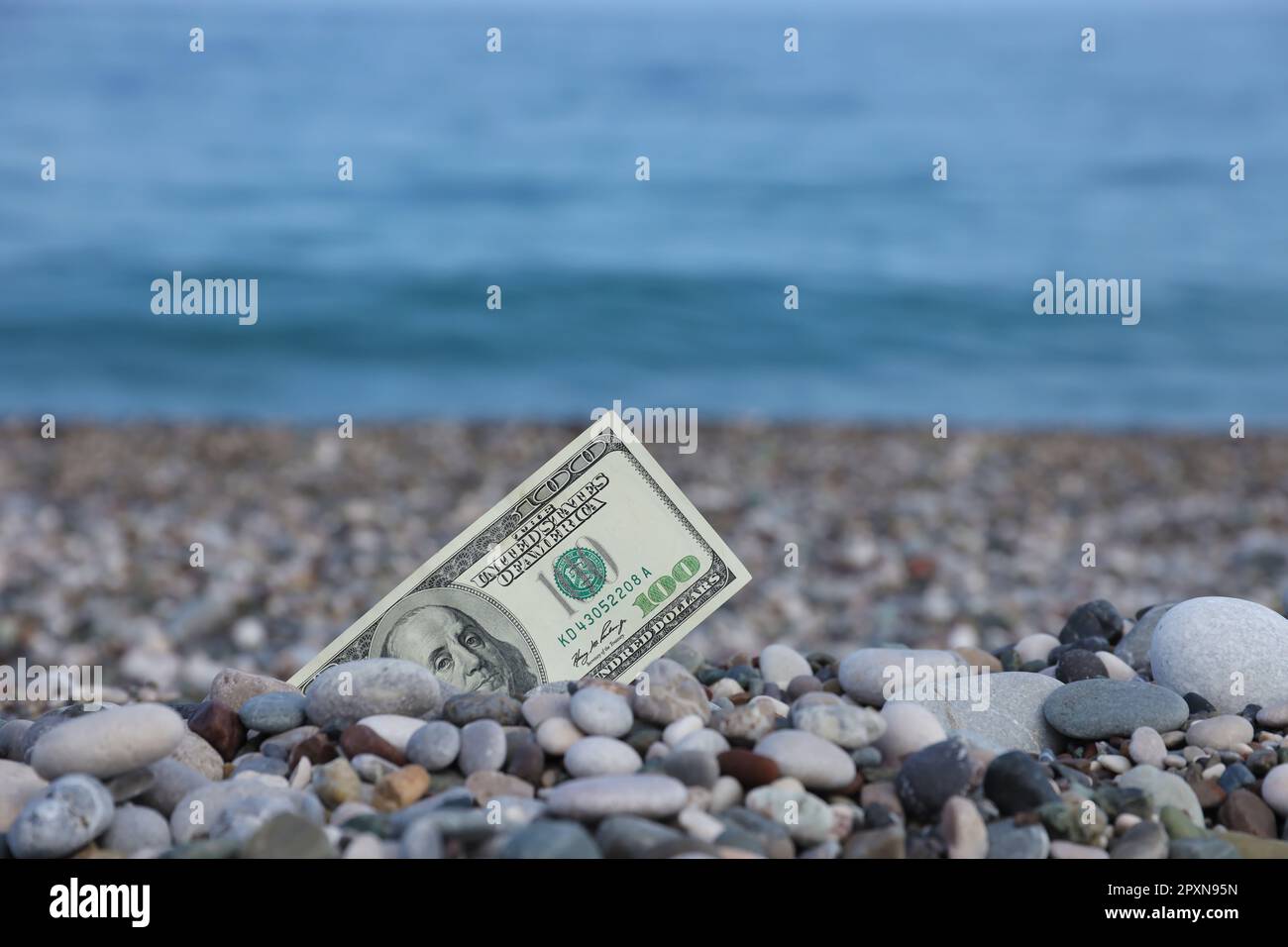 Hundred dollars half covered with round rocks lie on beach close up ...