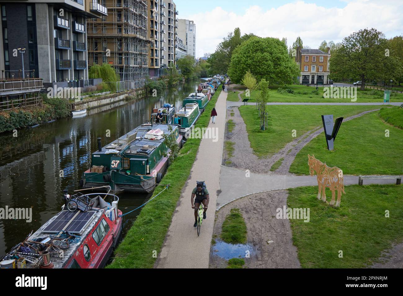 A cyclist rides past narrow boats on the towpath at The Regent's Canal ...