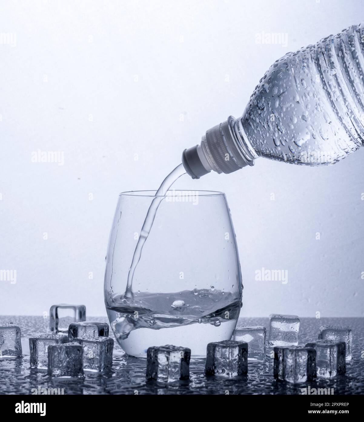 Pouring fresh drinking mineral water from plastic bottle. Glass filled with water over white ...