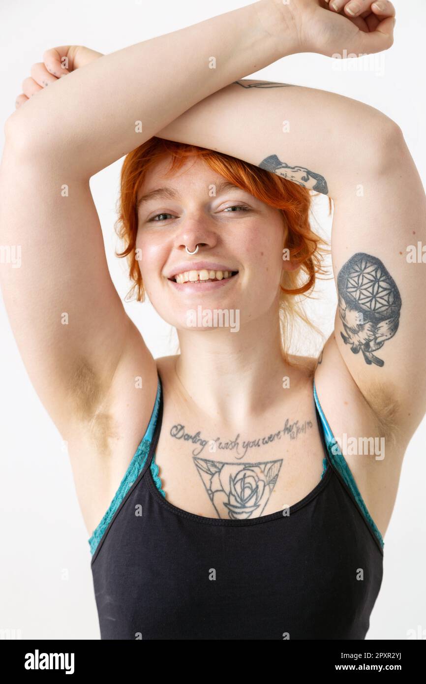 A beautiful woman in her mid twenties with tattoos and unshaved armpits with her arms raised ...