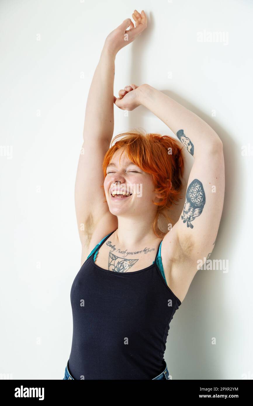 A beautiful woman in her mid twenties with tattoos and unshaved armpits with her arms raised ...