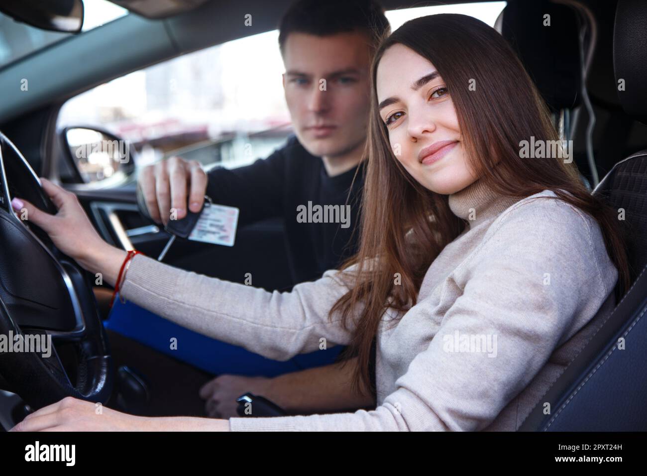 Happy girl in a new car receives a drivers license and keys from a ...