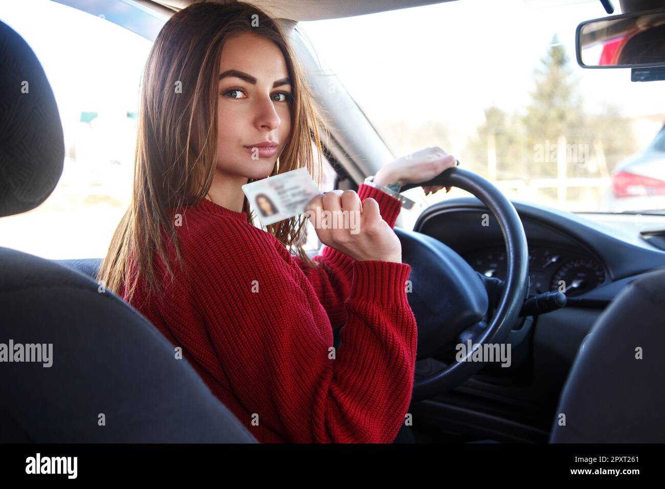 Joyful girl driving a training car with a drivers license card in her ...