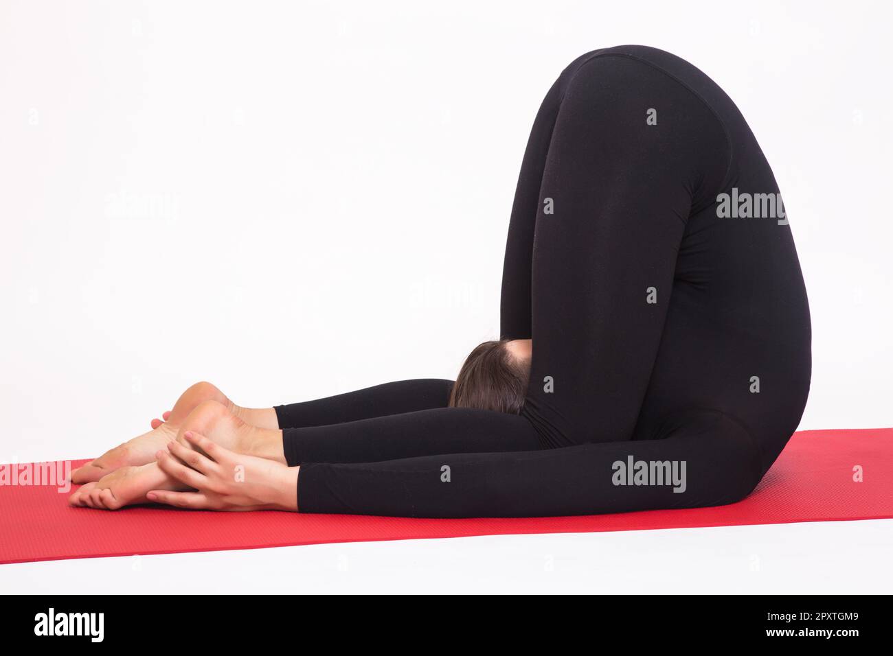 Beautiful athletic girl in a black suit doing yoga. karnapidasana asana ...