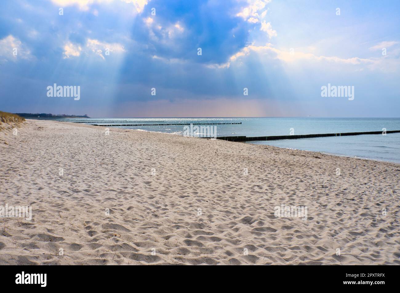 Sun rays shine through dense clouds on the beach of the Baltic Sea. Groynes on the coast. Sandy ...