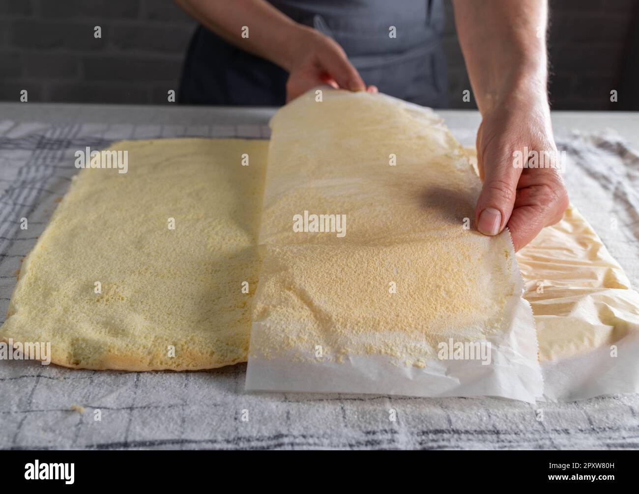 Removing baking paper from a fresh baked sponge cake for making swiss ...
