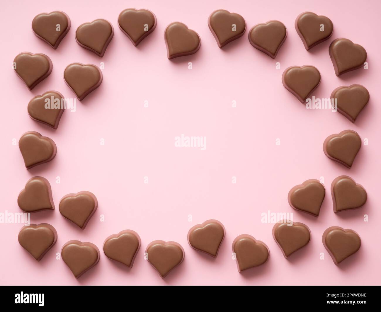 Frame of romantic chocolate confections in heart shapes on pastel pink ...