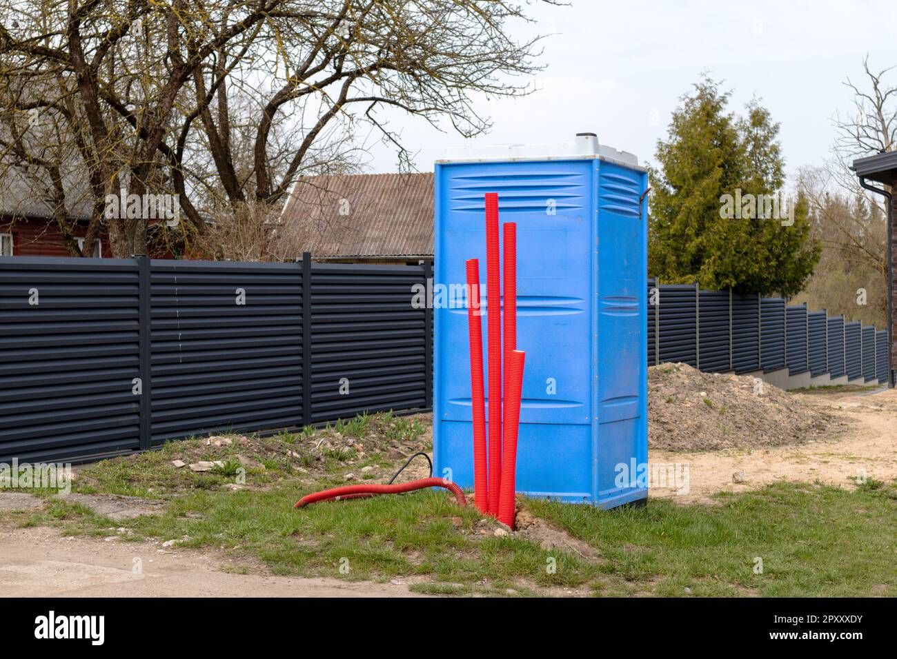 A blue plastic WC cabin on the construction site and red water drainage ...