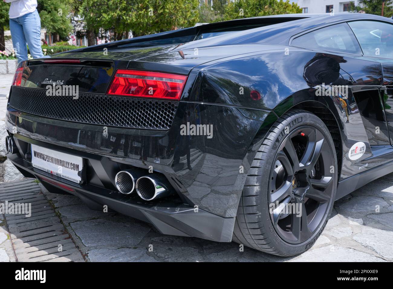 A young adult man stands in front of a classic black Lamborghini sports ...