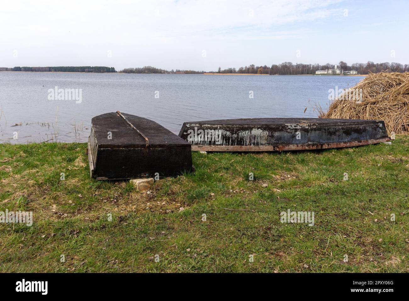 A small boat laid upside down on the grass next to the lake Stock Photo ...