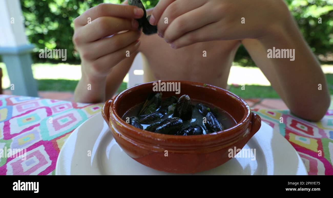 Child eating seafood mussels on bowl outside during summer day. Young ...
