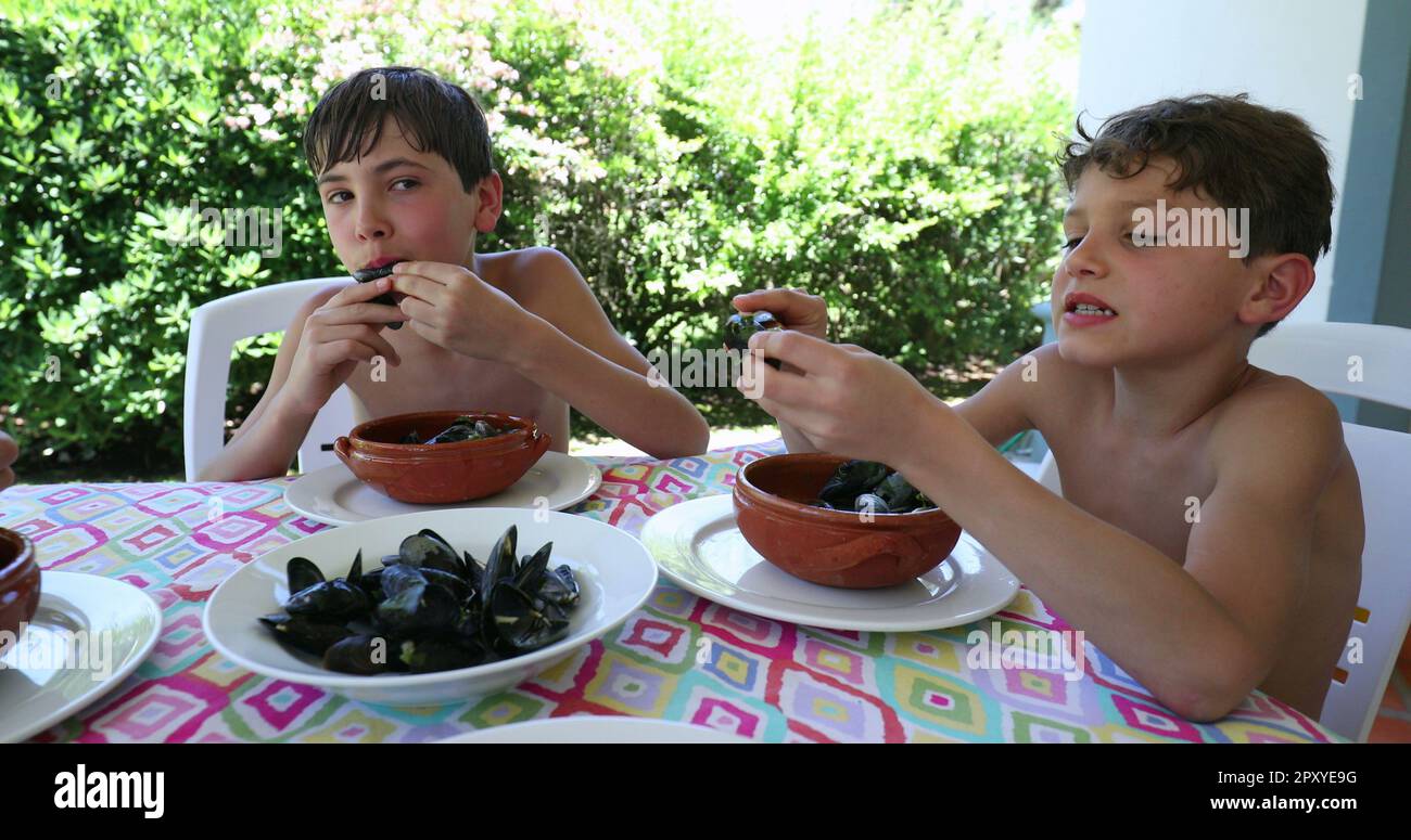 Children eating seafood mussels. Kids at lunch table tasting moules ...