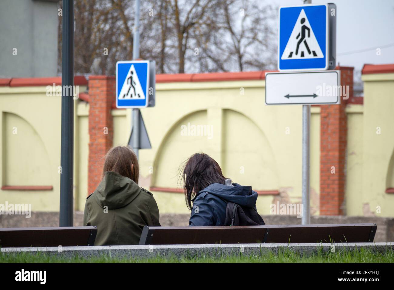 Two people sitting on a bench, one of them has a blue sign that says ...
