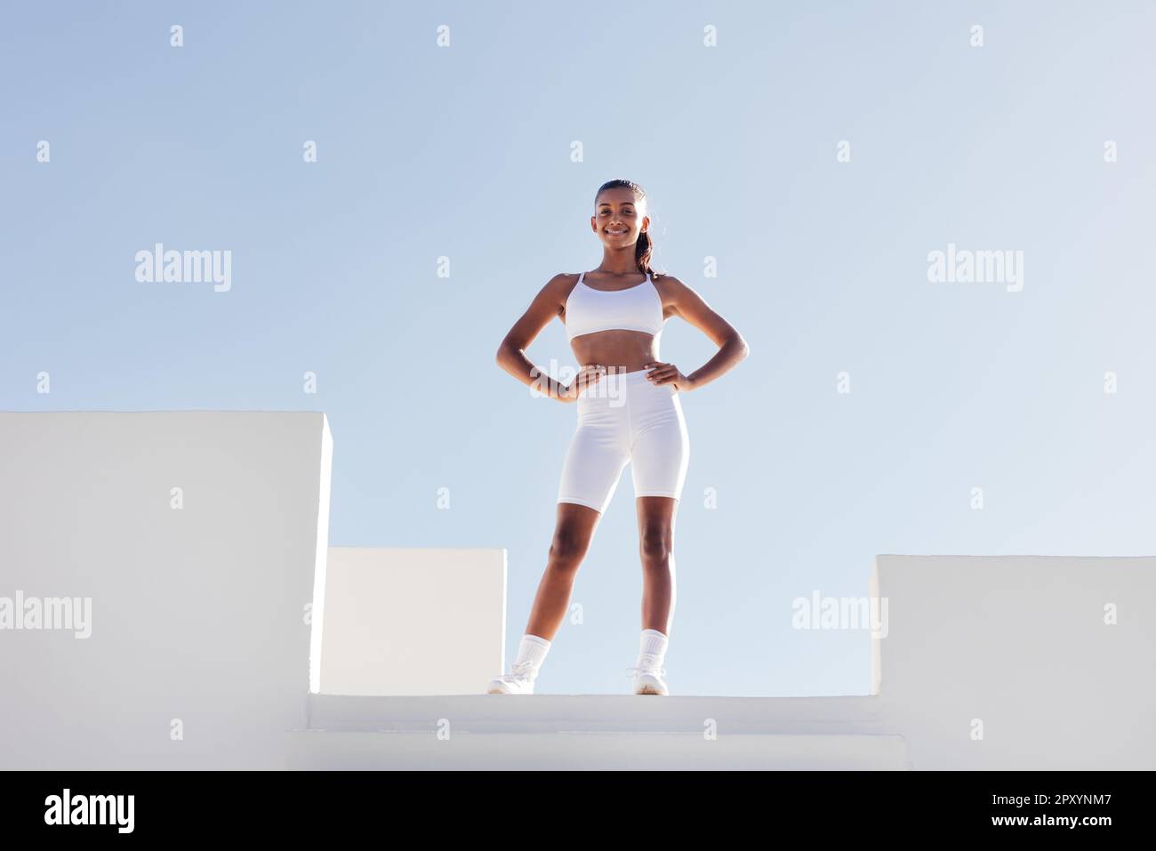 Slim smiling woman in white fitness attire posing on a top of stairs ...