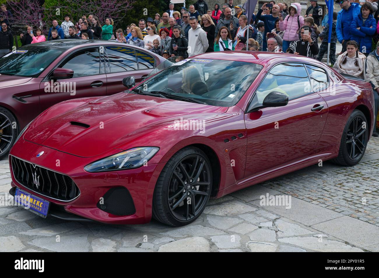 Two bright red Maserati cars parked side-by-side on a public street ...