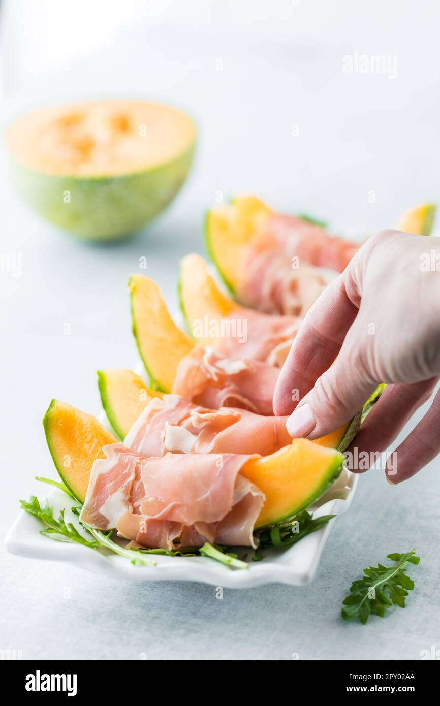 A hand reaching in to grab a prosciutto wrapped cantaloupe slice from a ...