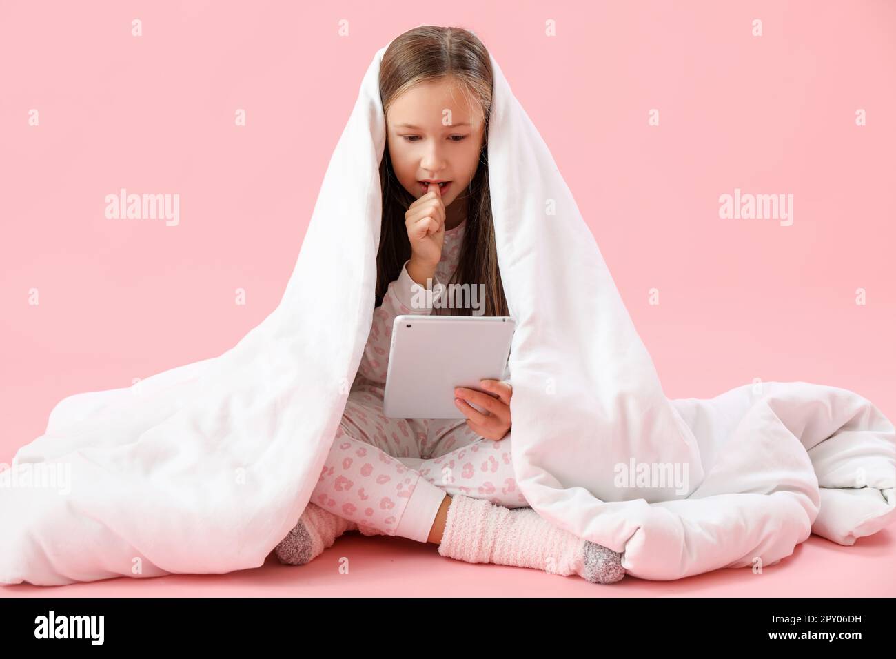 Little girl with blanket and tablet computer biting nails on pink ...