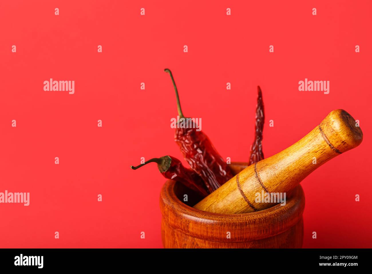 Wooden mortar and pestle with dry chili pepper on red background ...