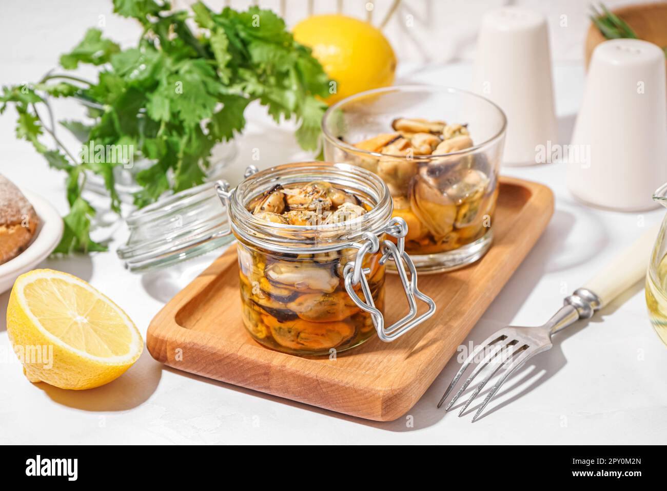 Board with jar and glass bowl of pickled mussels on white background ...