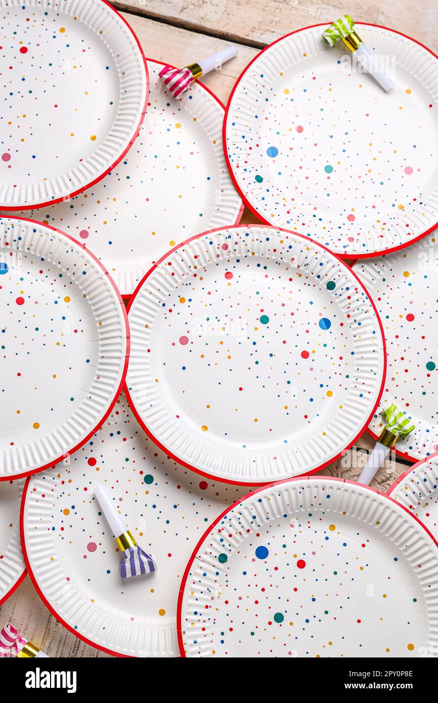 Paper disposable plates with party blowers on light wooden background ...