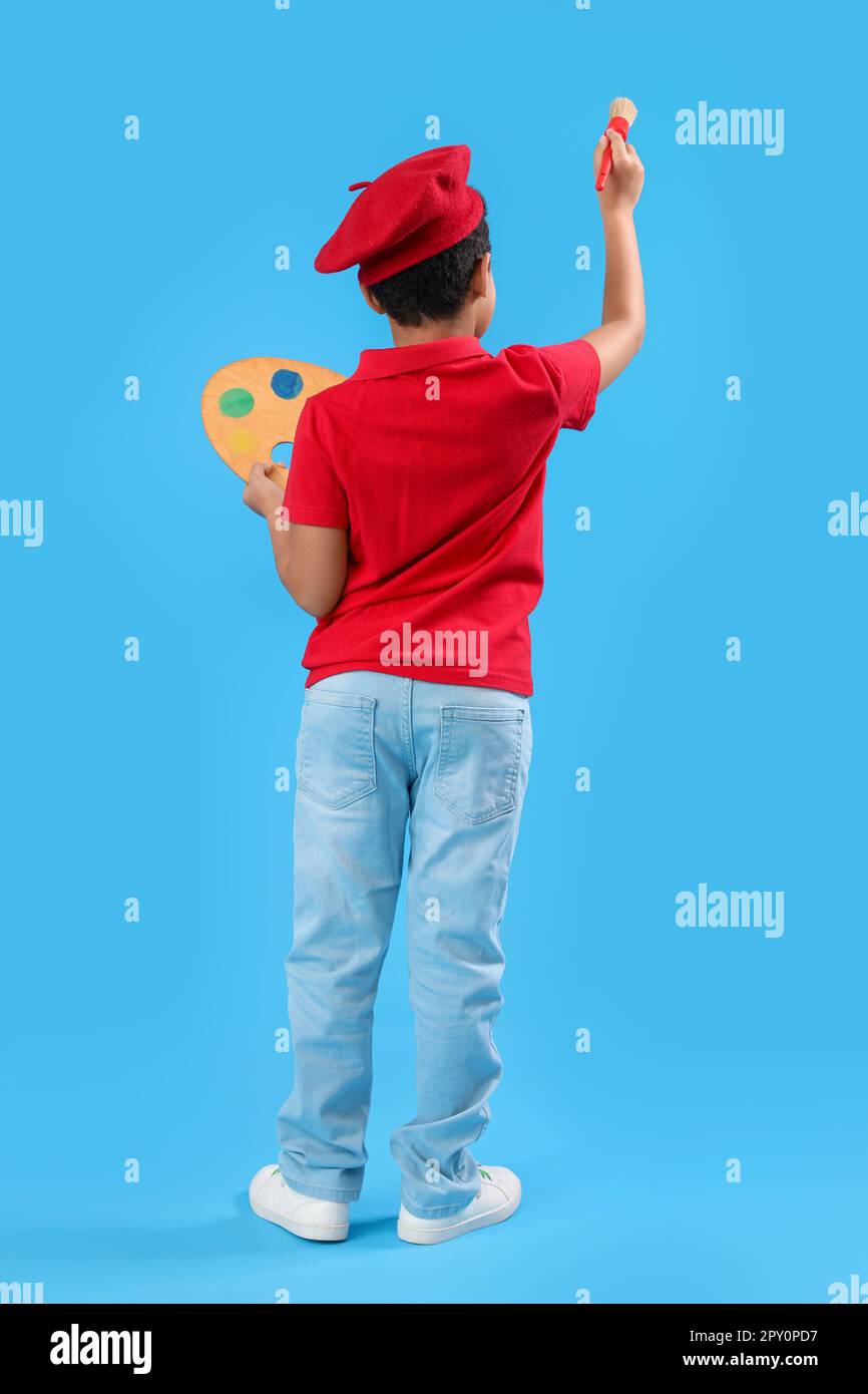 Little artist with brush and paint palette on blue background, back ...