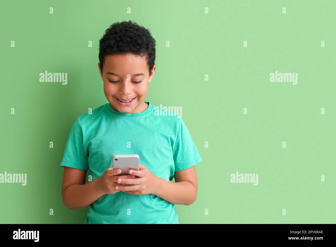 Little African-American boy using mobile phone on green background ...