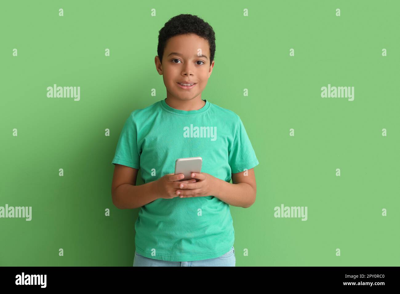 Little African-American boy using mobile phone on green background ...