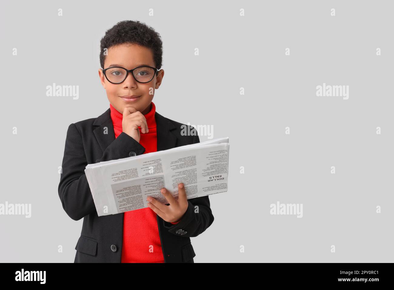 Little African-American boy reading newspaper on light background ...