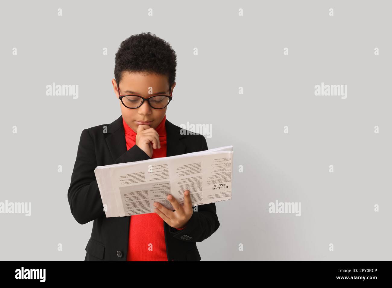 Little African-American boy reading newspaper on light background ...
