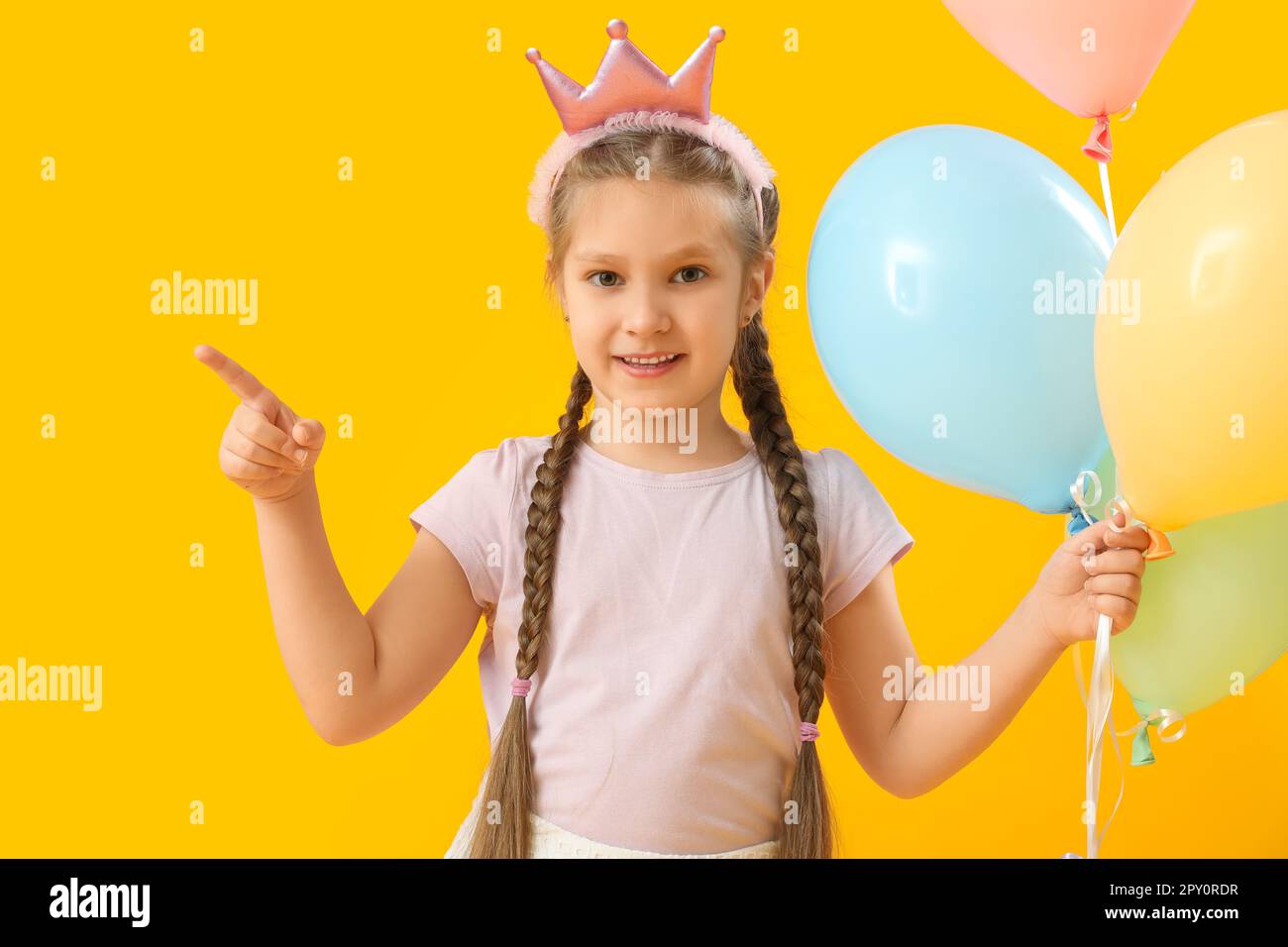 Little girl in crown with balloons pointing at something on yellow ...