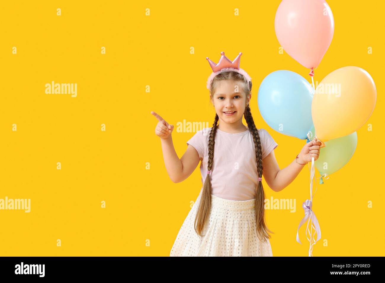 Little girl in crown with balloons pointing at something on yellow ...