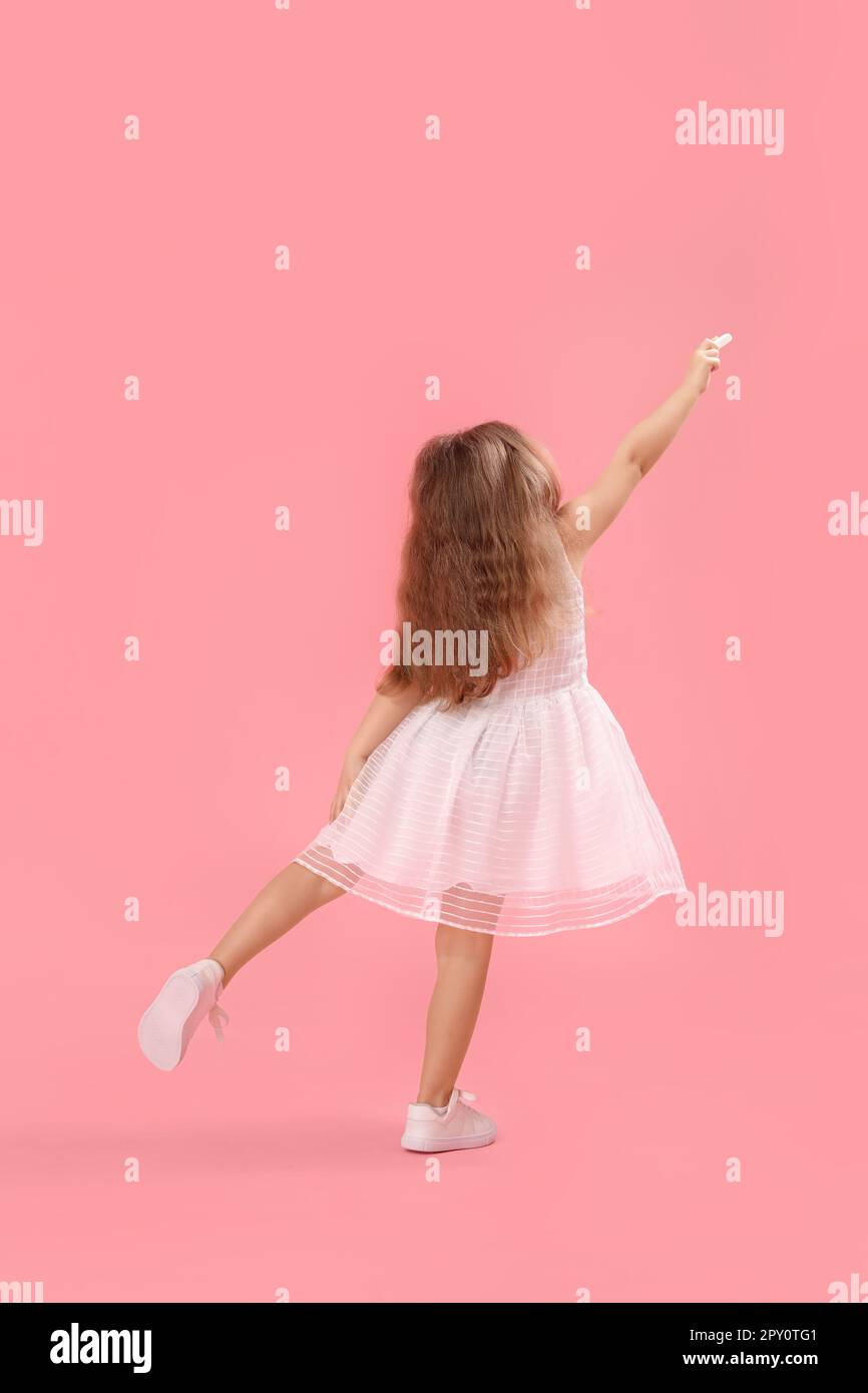 Little girl drawing with chalk piece on pink background, back view ...
