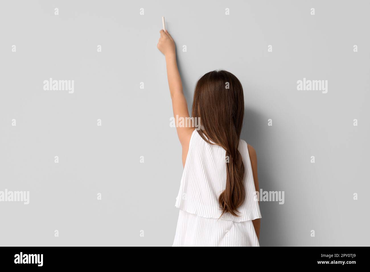 Little girl drawing with chalk piece on light background, back view ...