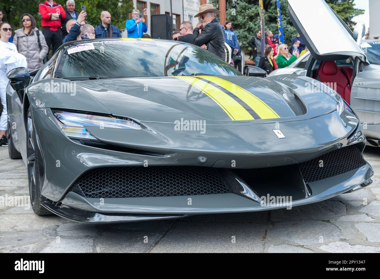 A group of people gathered around grey Ferrari with yellow racing ...
