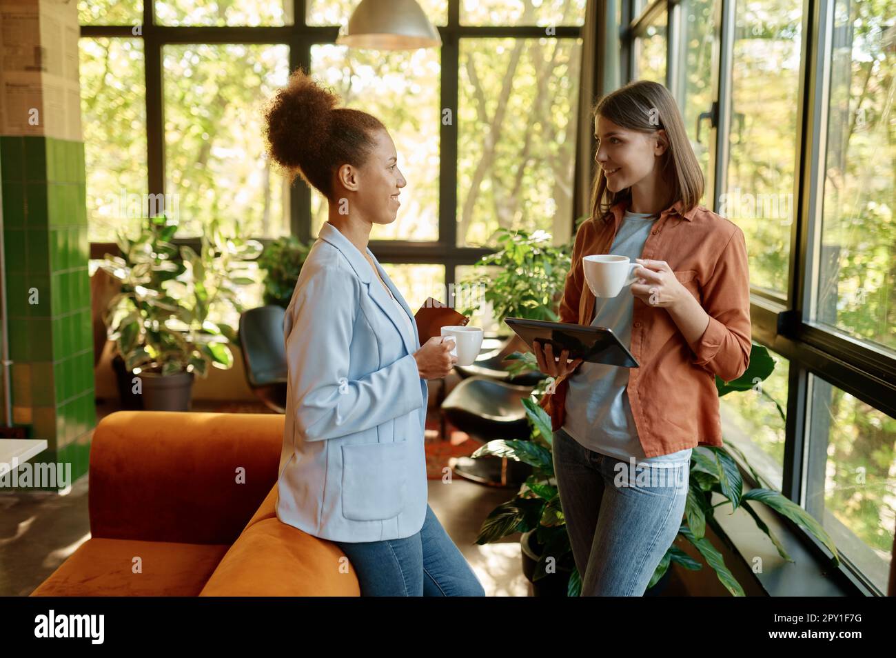 Happy cheerful coworkers chatting and laughing at workplace. Two female ...